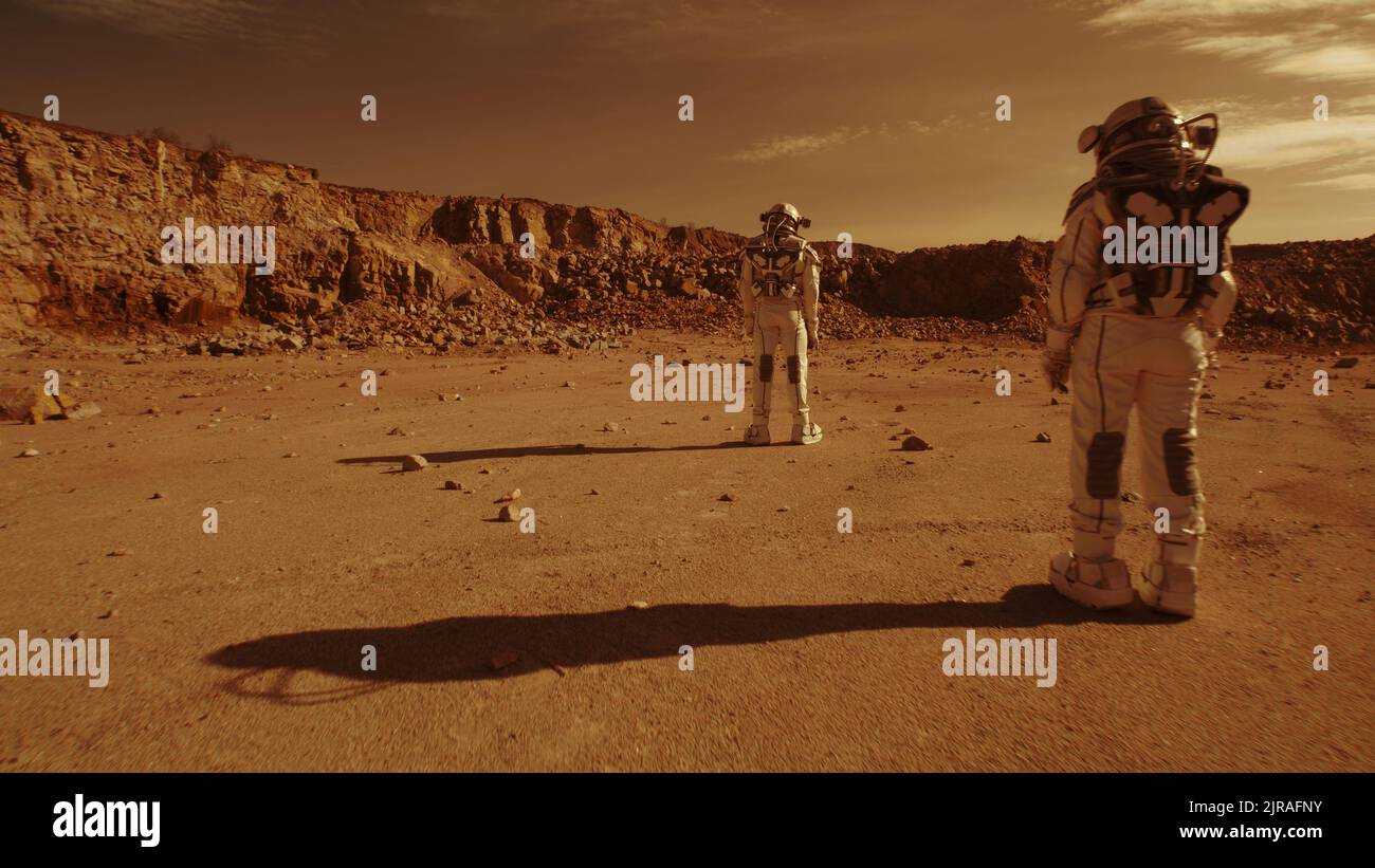 Zoom in view of people in spacesuits standing in arid valley and ...