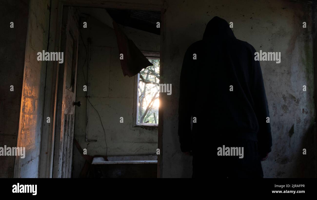 A spooky strange concept of a hooded man back to camera facing a wall ...