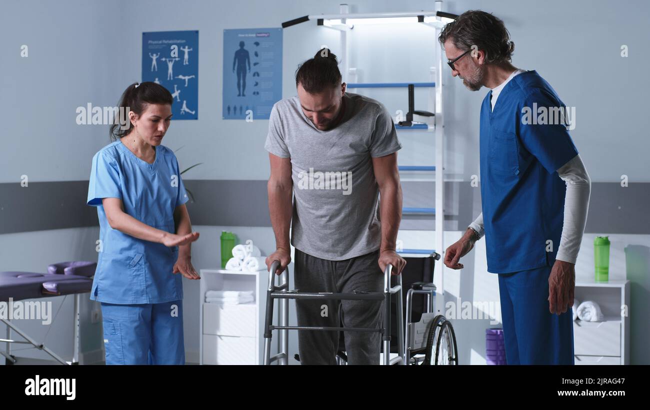 Female and male therapist helping adult patient on wheelchair to stroll ...