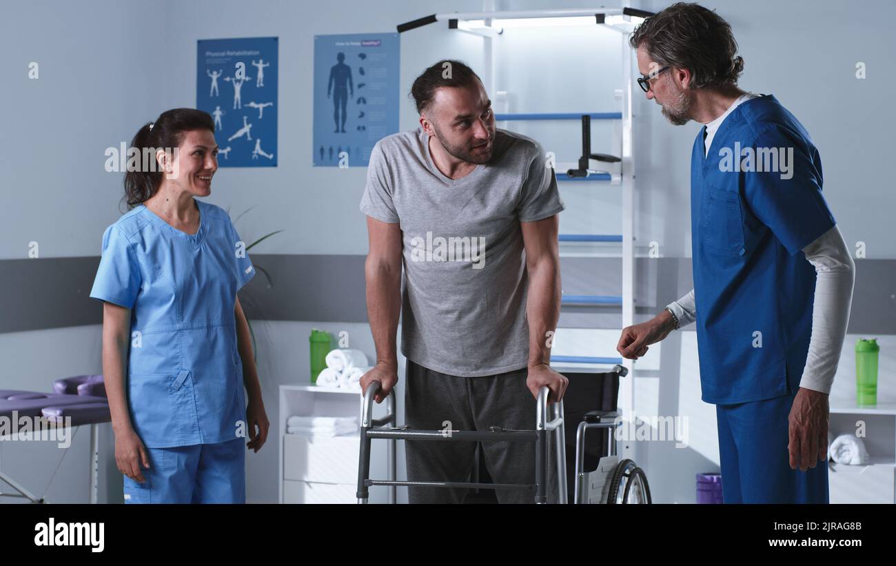 Female and male therapist helping adult patient on wheelchair to stroll ...