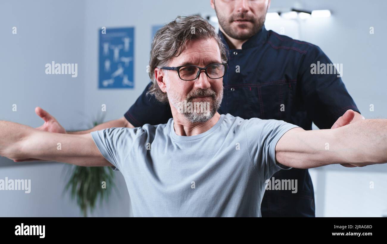 Man supporting middle aged male patient doing exercise with dumbbells ...