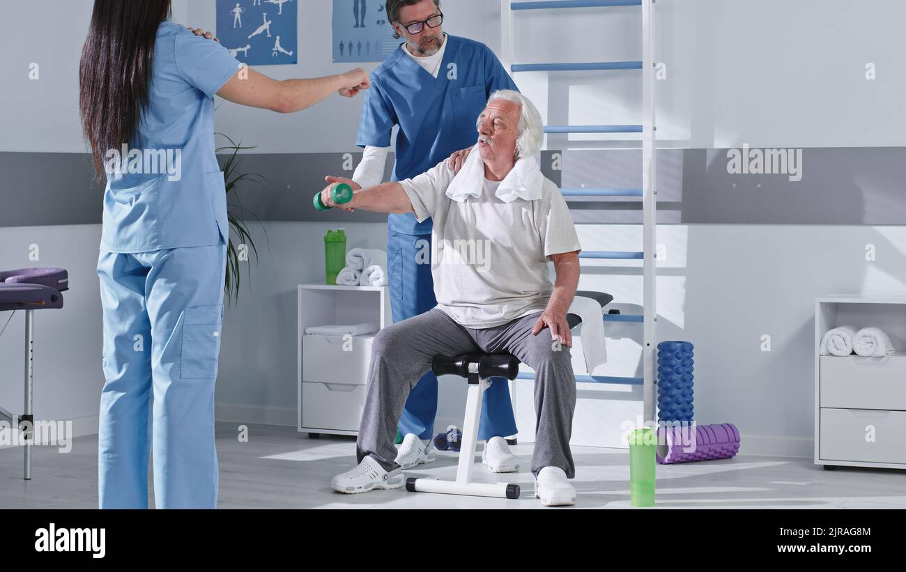 Male and female rehabilitation therapists showing and helping senior ...