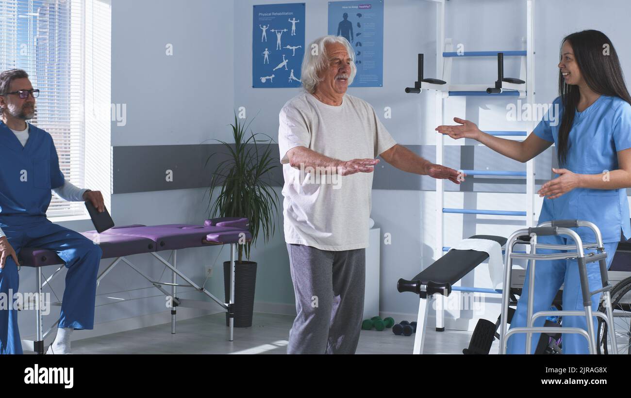 Adult woman helping senior male patient to stroll without walking frame ...