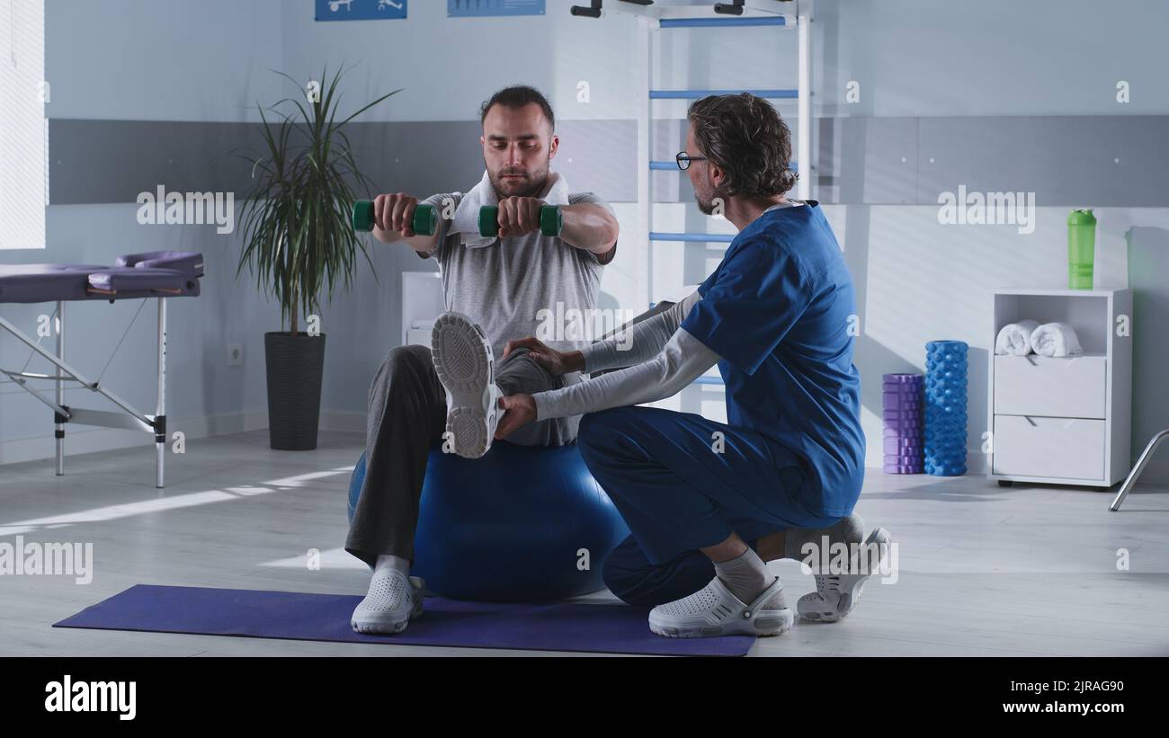 Middle aged man in medical uniform supporting adult male patient with ...