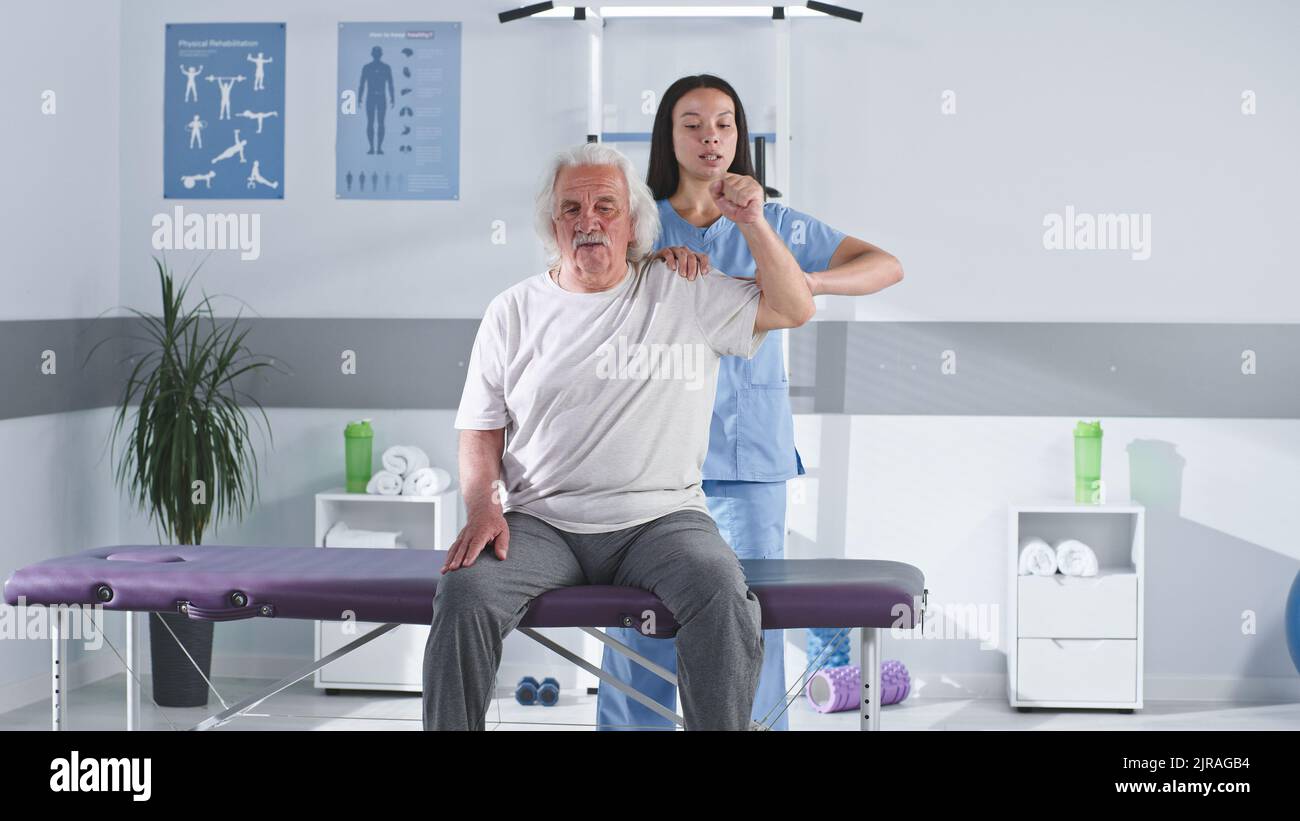 Female doctor stretching arm of relieved senior male patient during ...