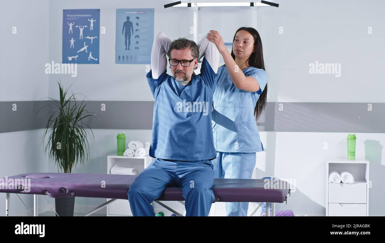 Female doctor stretching arms and shoulders of middle aged man while ...
