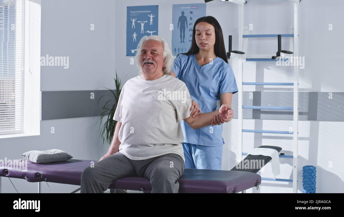 Female doctor stretching arm of relieved senior male patient during ...