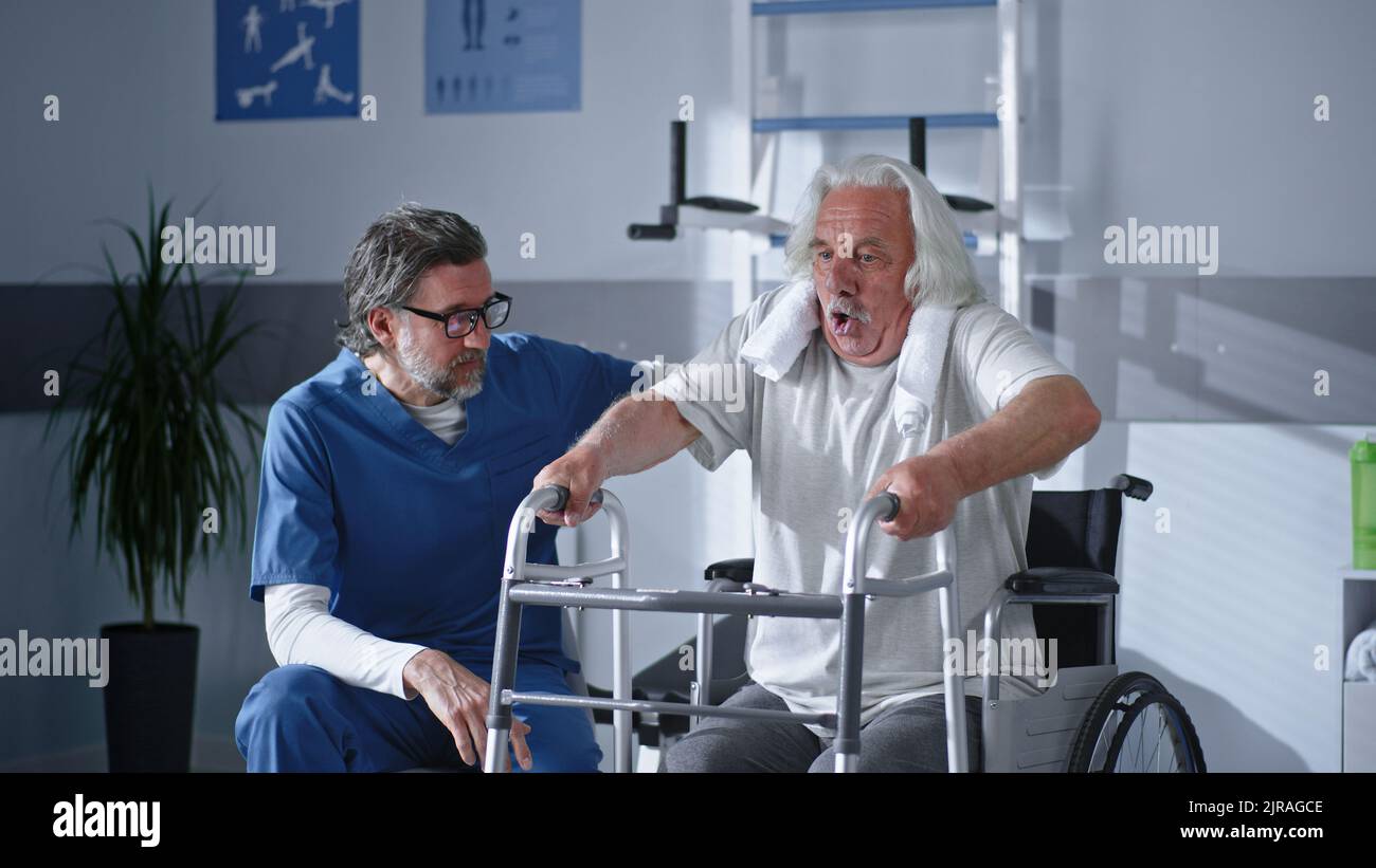 Optimistic aged man standing up from wheelchair and trying to stroll ...