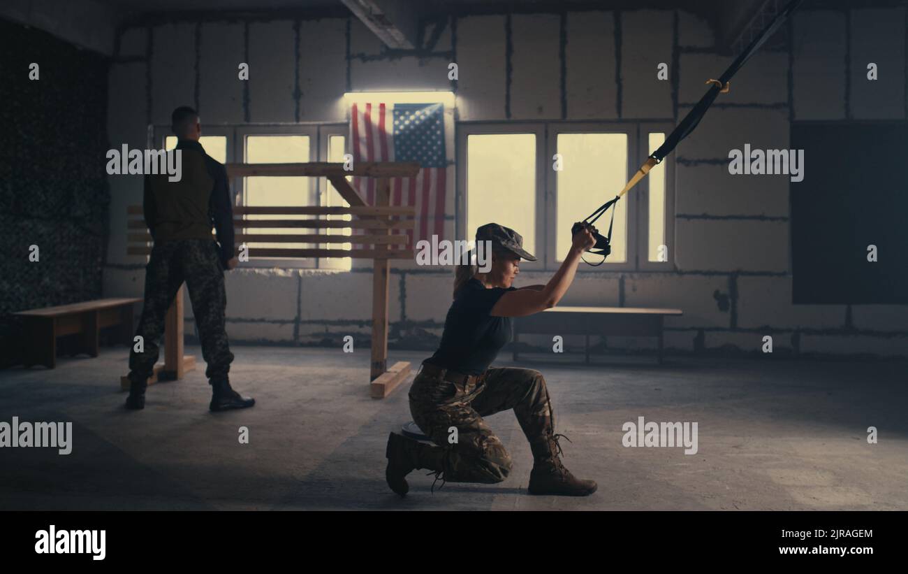 View of tired woman in camouflage pants doing TRX lunges near squadmate ...