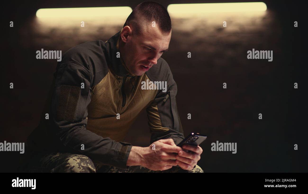 Male soldier using mobile phone to make video call while sitting in ...