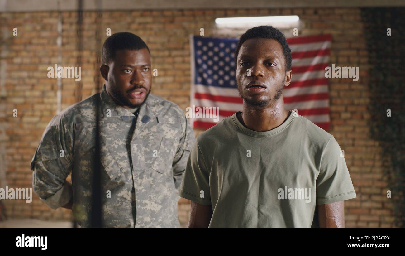Black instructor talking to male soldier exercising with TRX ropes ...