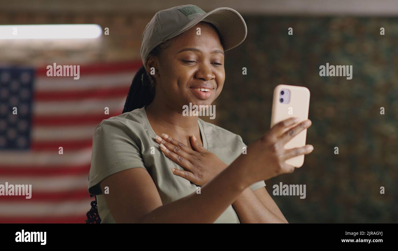 Happy black woman smiling and waving hand while using smartphone to speak with online friend on ...