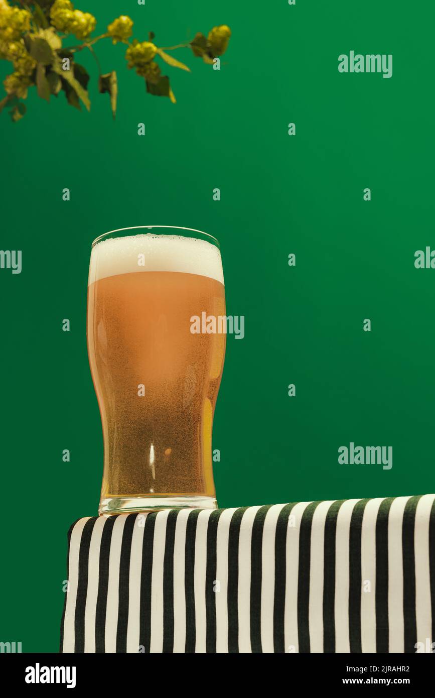 Glass of cold frothy light beer over dark green background with hop ...