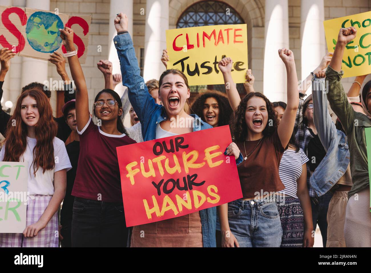 Group of multicultural youth activists shouting slogans and raising their fists during a climate ...