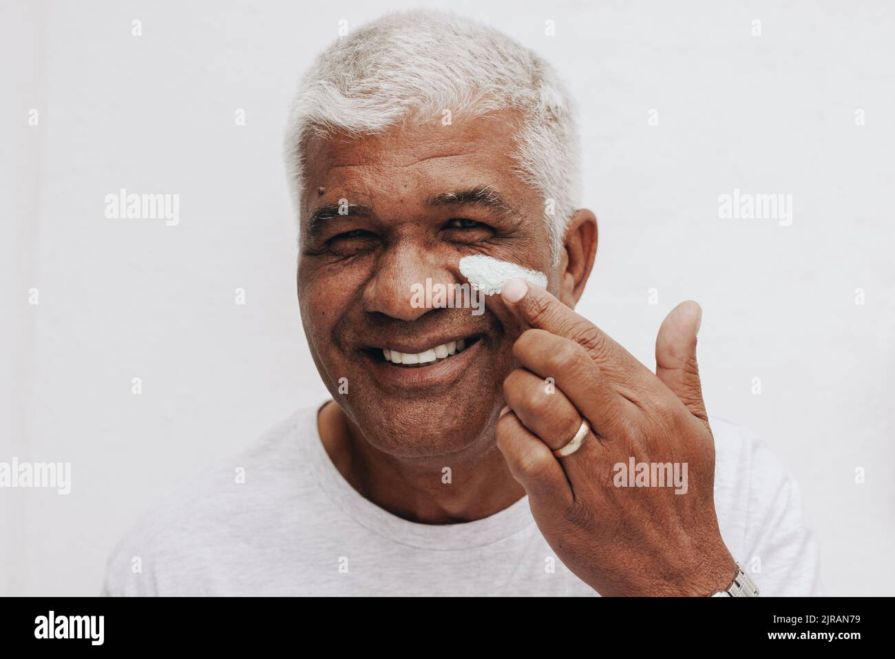 Happy senior man smiling at the camera while applying a moisturizing ...