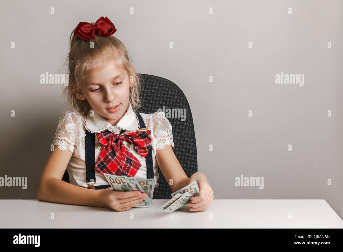 A little girl in a school uniform is counting money - hundred-dollar ...