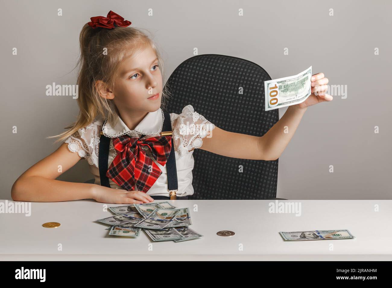 A little girl sits at a table in front of a stack of hundred-dollar ...