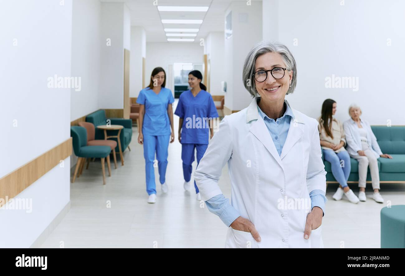Friendly female general practitioner wearing medical uniform standing ...