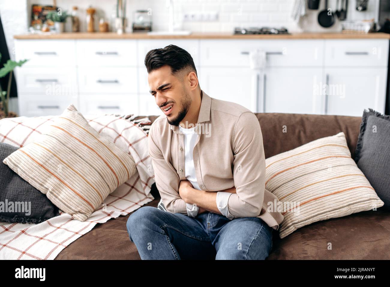 Frustrated unhealthy indian or arabian young man, sitting on the sofa ...