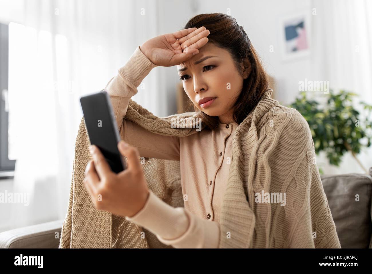 sad sick woman in blanket using smartphone at home Stock Photo - Alamy