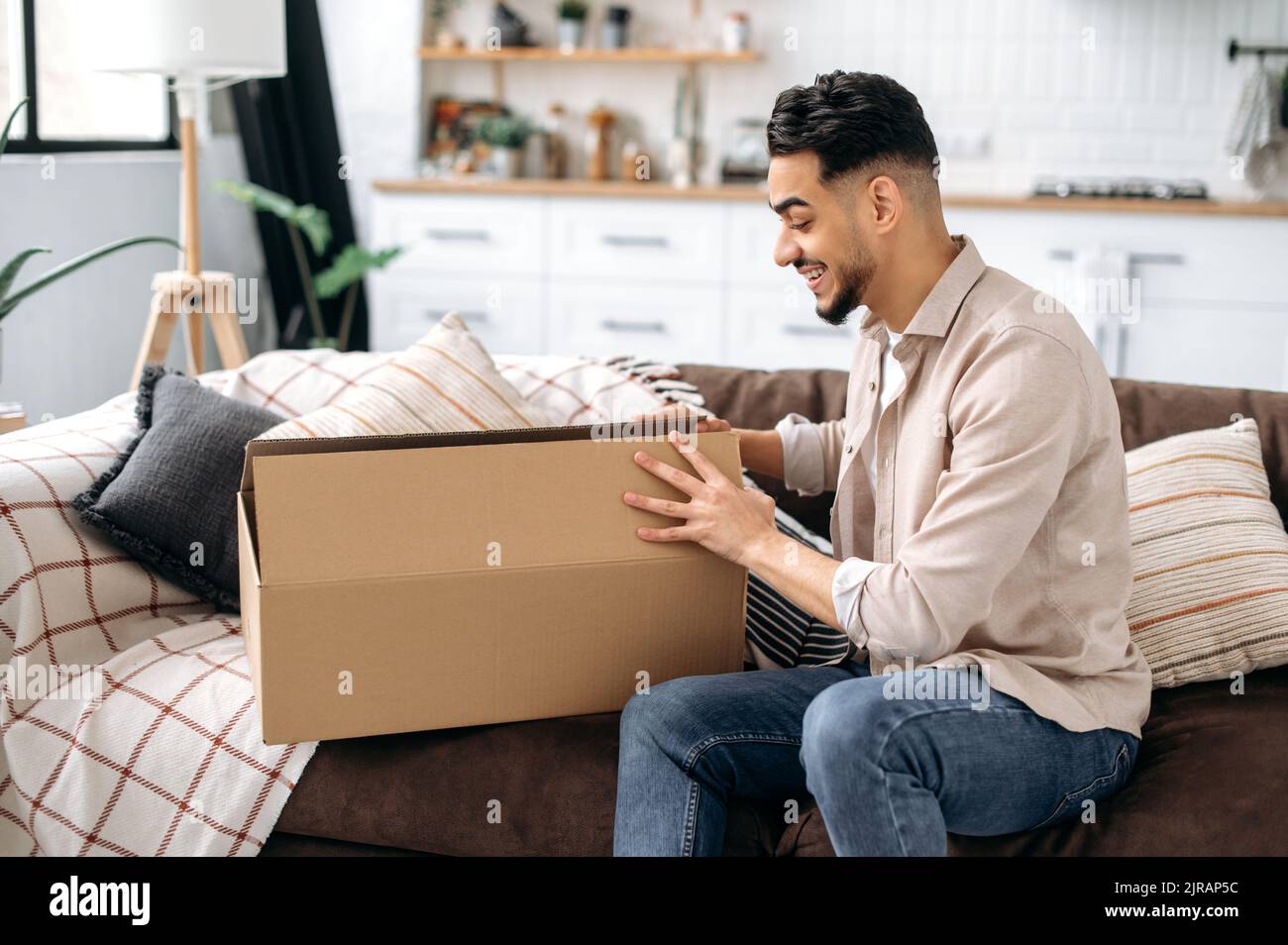 Excited mixed race young man opening big carton box, unpacking internet ...