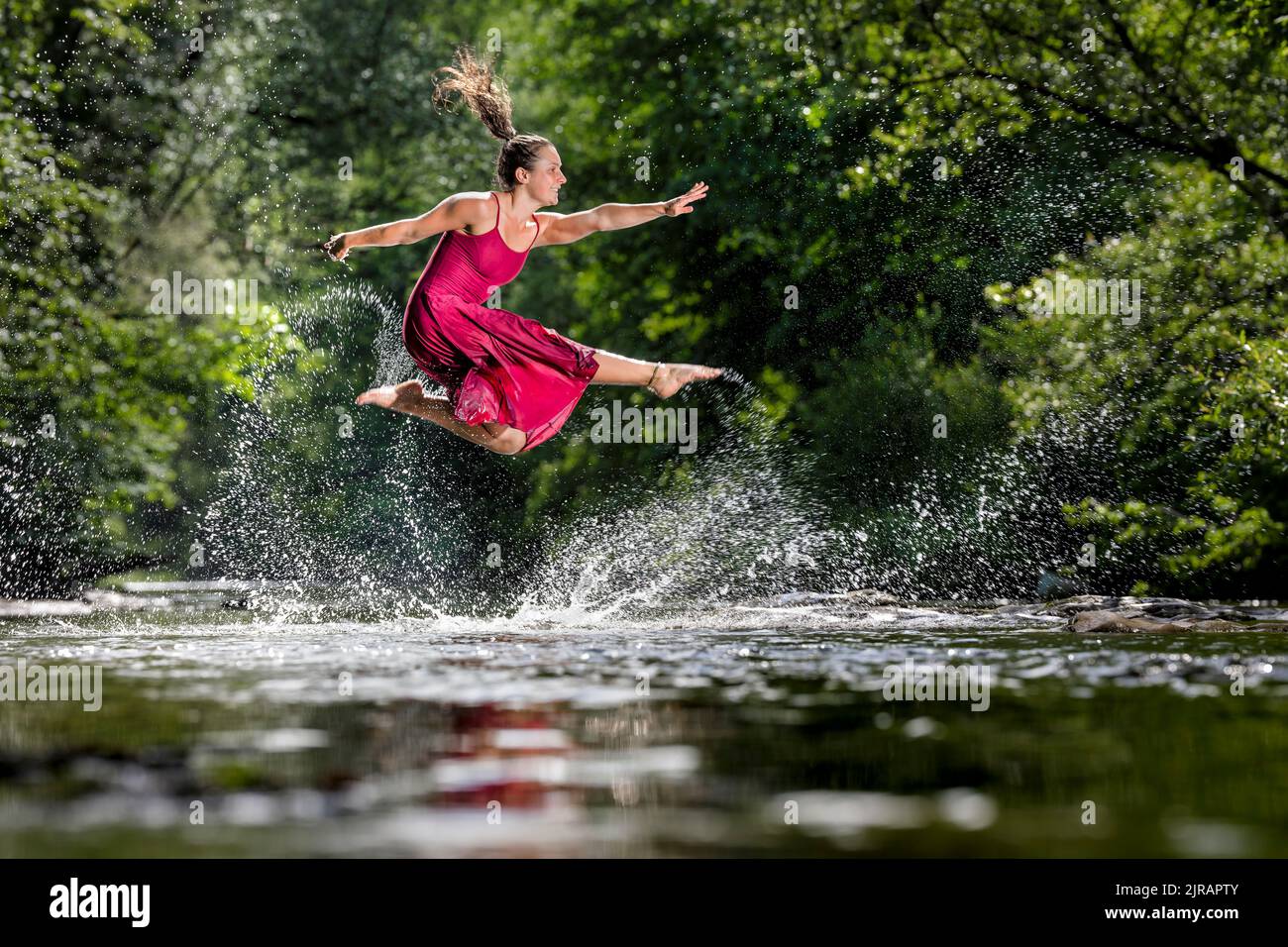 Woman with arms outstretched jumping over river Stock Photo - Alamy