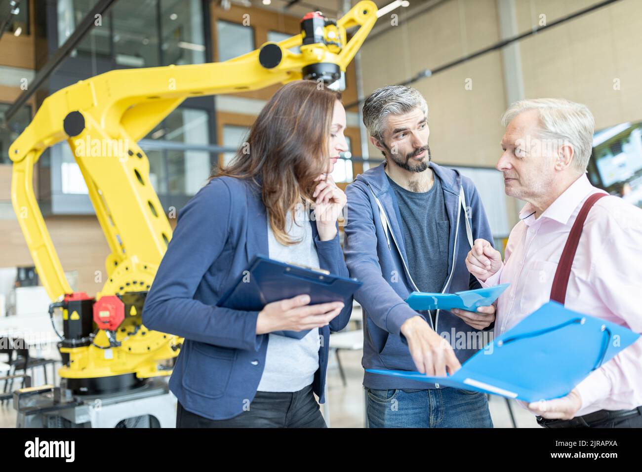 Engineers in factory having meeting in front of industrial robot Stock Photo - Alamy