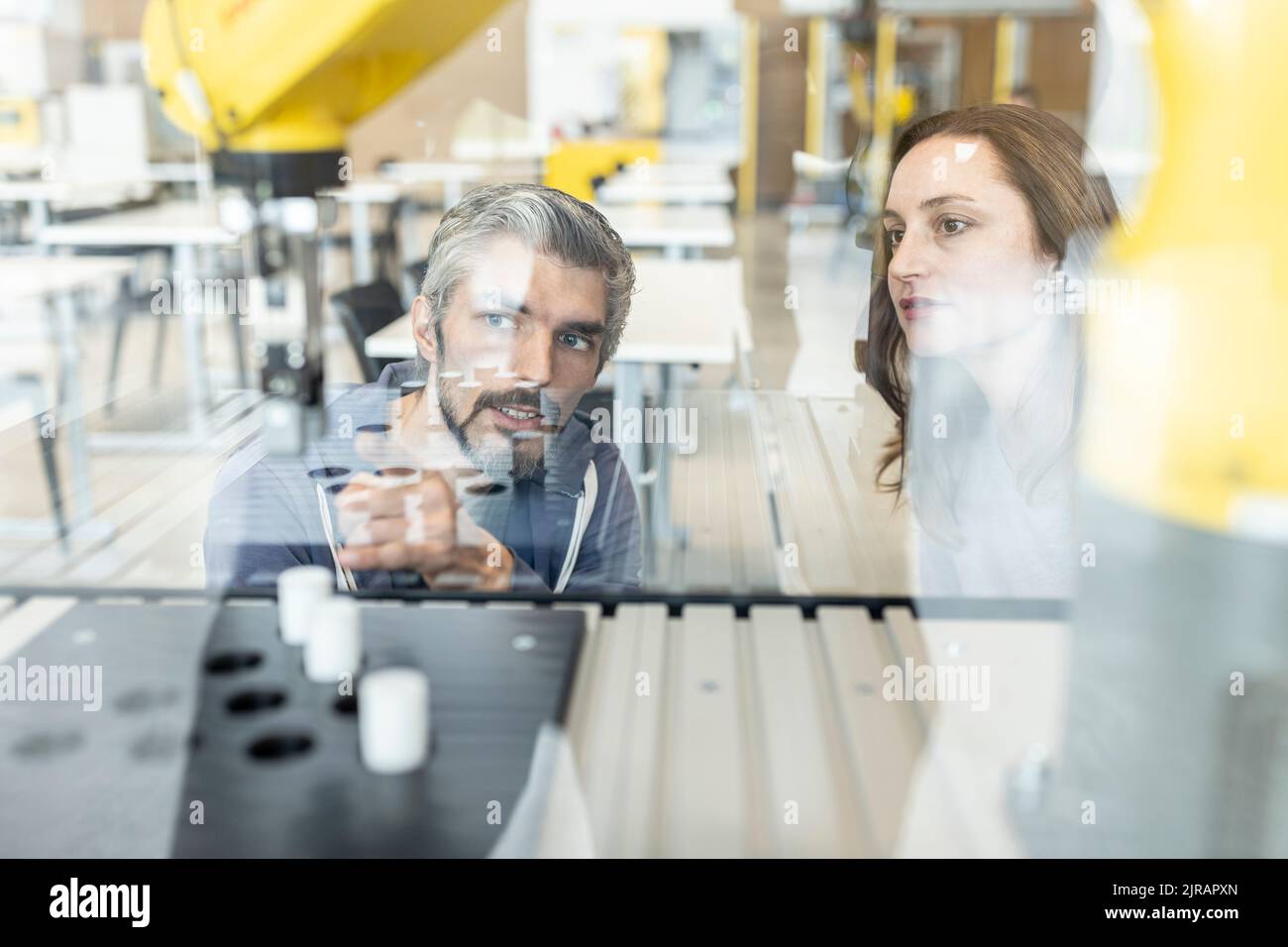 Engineers testing industrial robot in glass cabin Stock Photo - Alamy