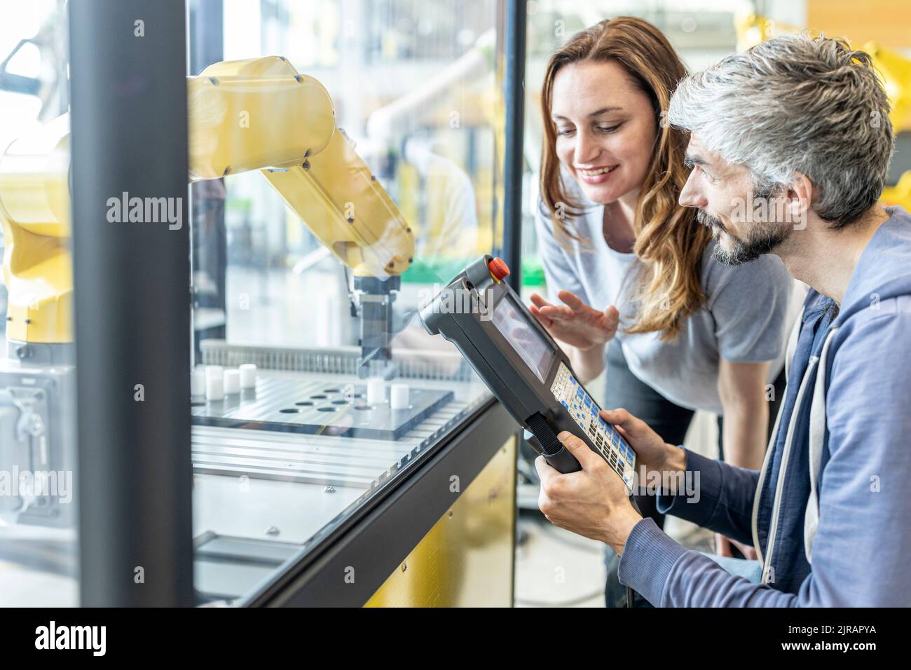 Engineers testing industrial robot in glass cabin Stock Photo - Alamy