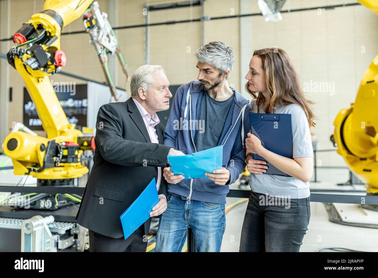 Manager discussing technical report with coworkers in front of industrial robot Stock Photo - Alamy