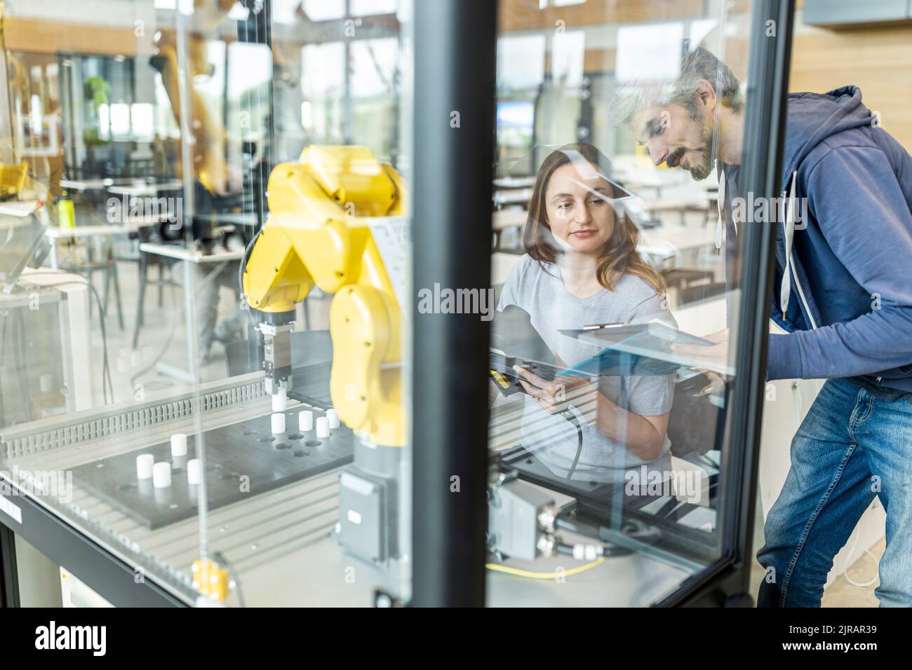 Engineers testing industrial robot in glass cabin Stock Photo - Alamy
