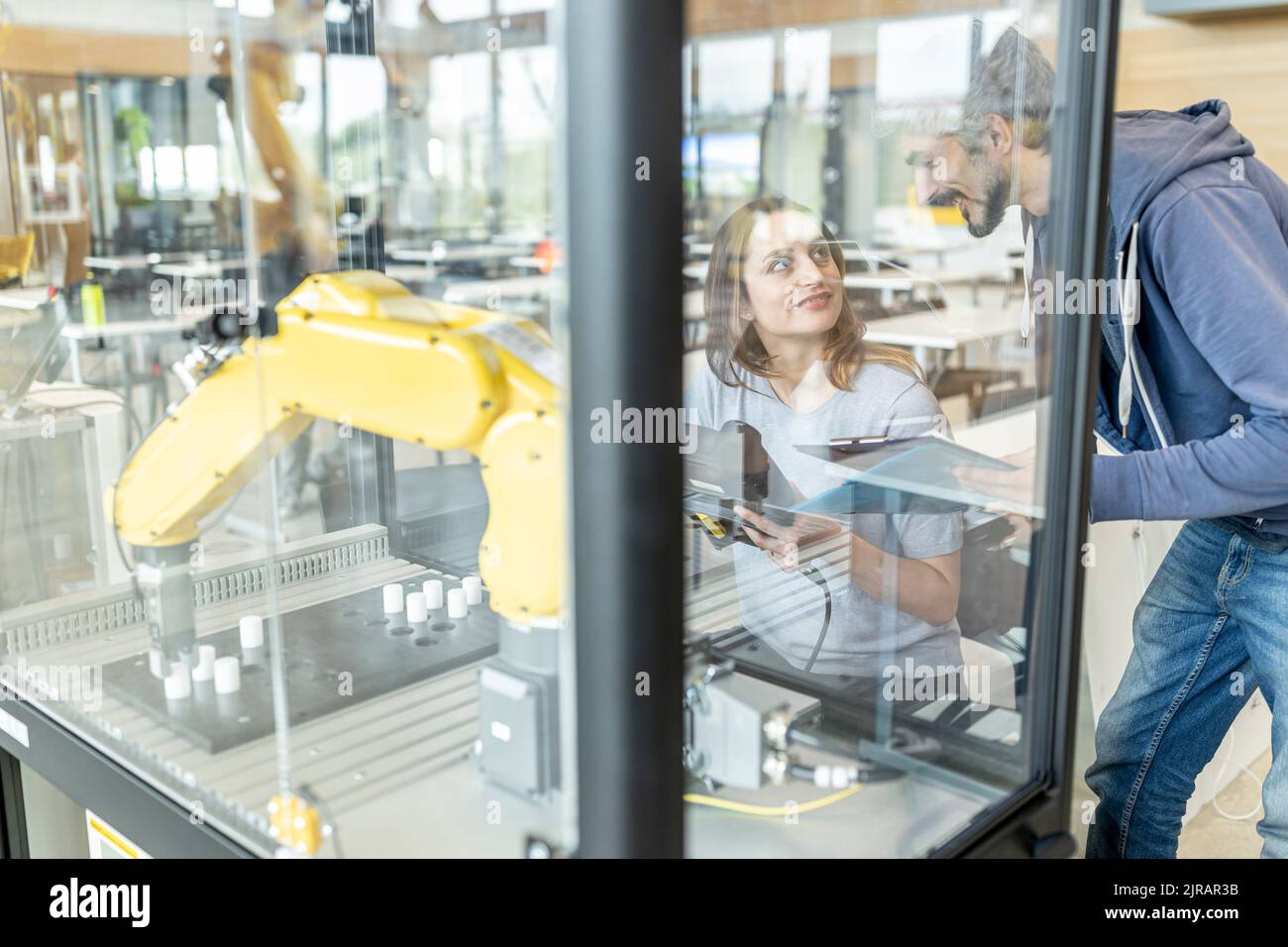 Engineers testing industrial robot in glass cabin Stock Photo - Alamy