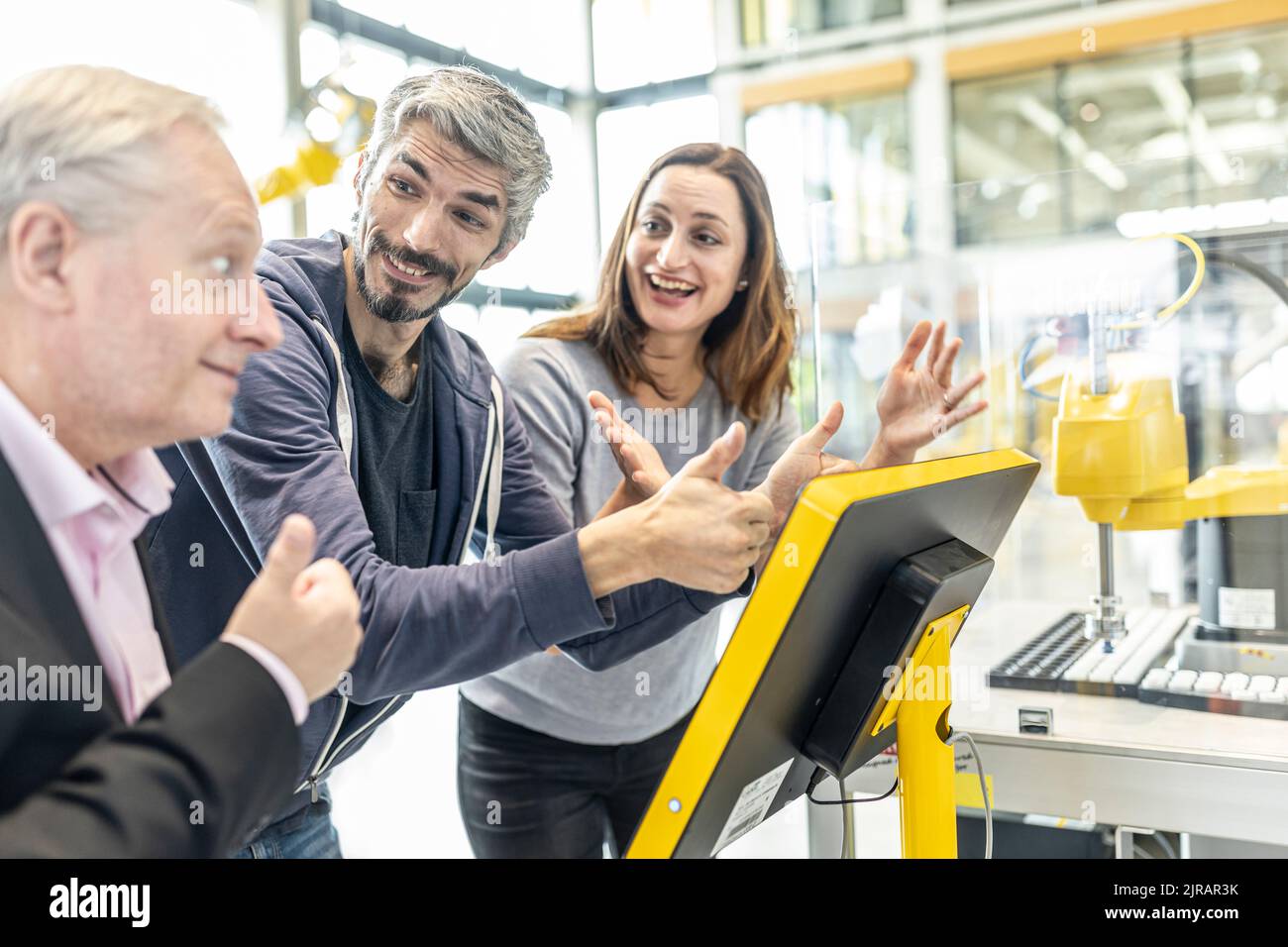 Happy colleagues giving thumbs up in robotic factory Stock Photo - Alamy