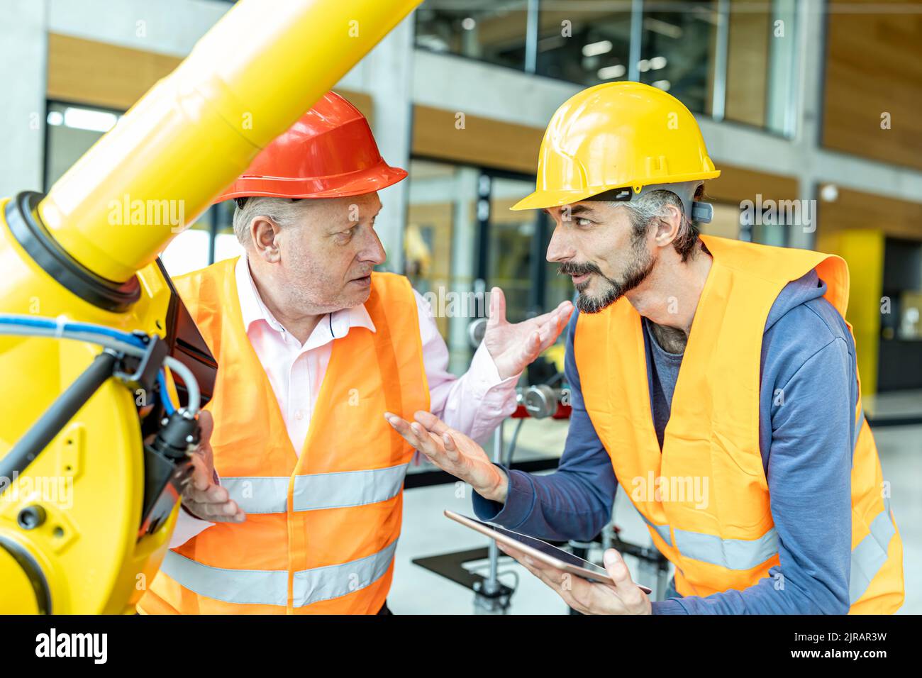 Male and female colleagues discussing robotic machine in industrial ...