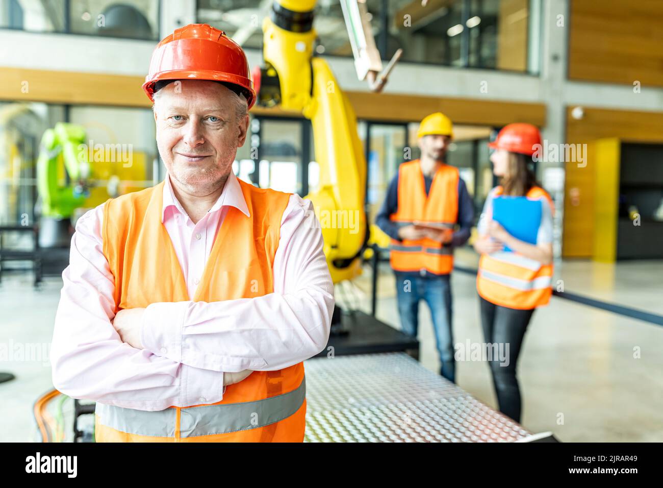 Confident industrial worker standing in robotic factory with arms ...