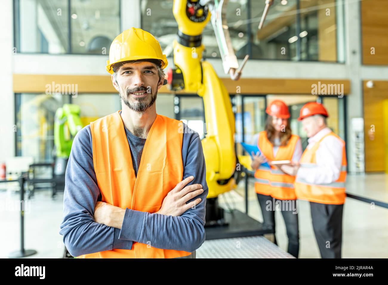 Confident industrial worker standing in robotic factory with arms ...