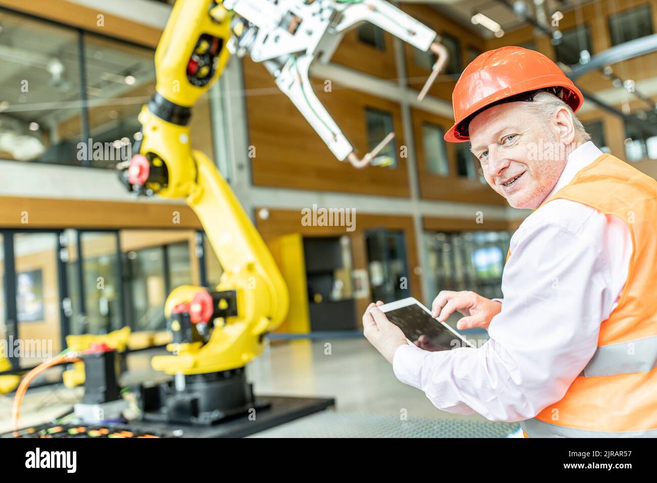 Confident skilled worker controlling robot arm with digital tablet ...