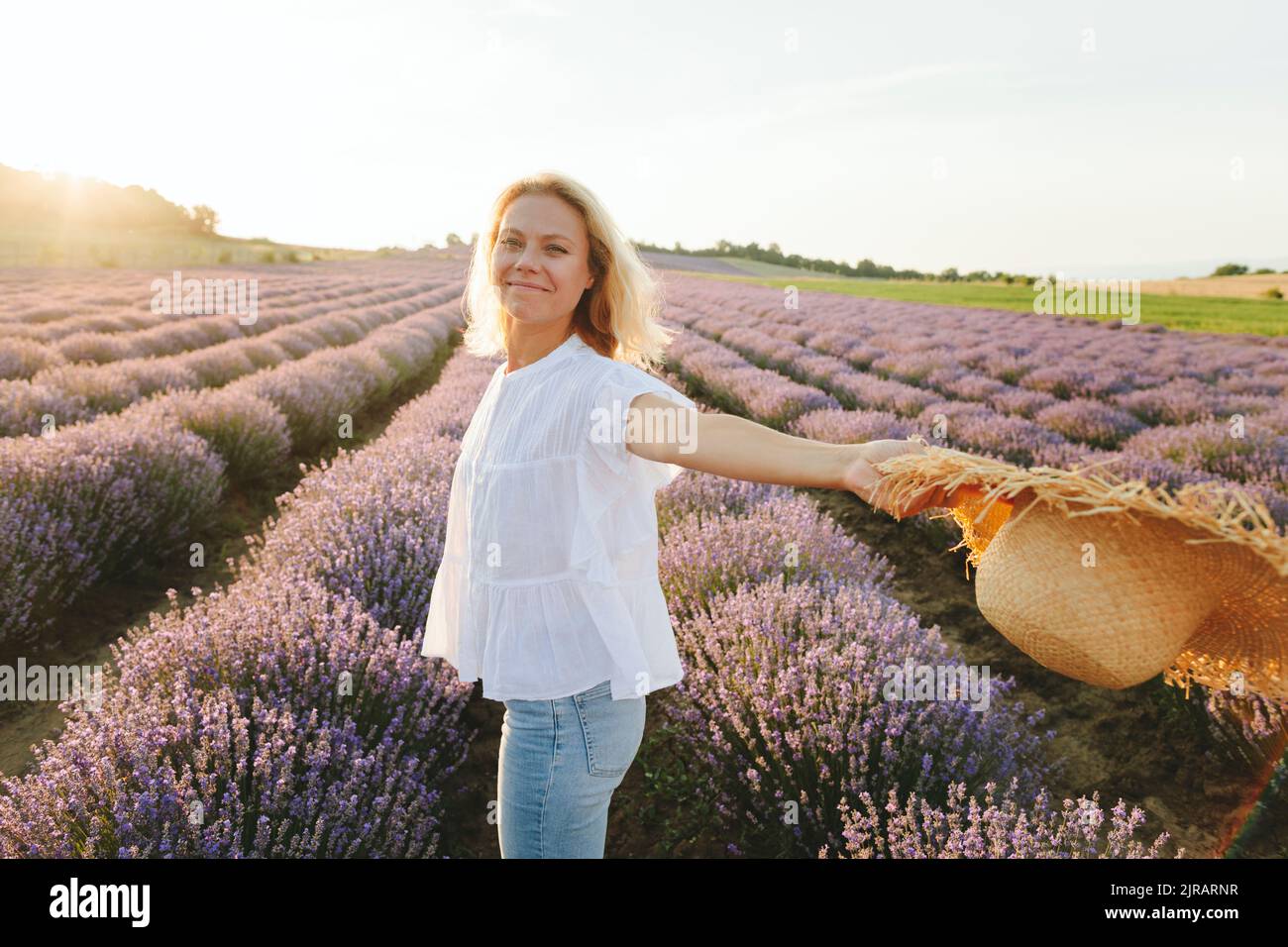 Carefree woman with straw hat enjoying in lavender field at sunset ...