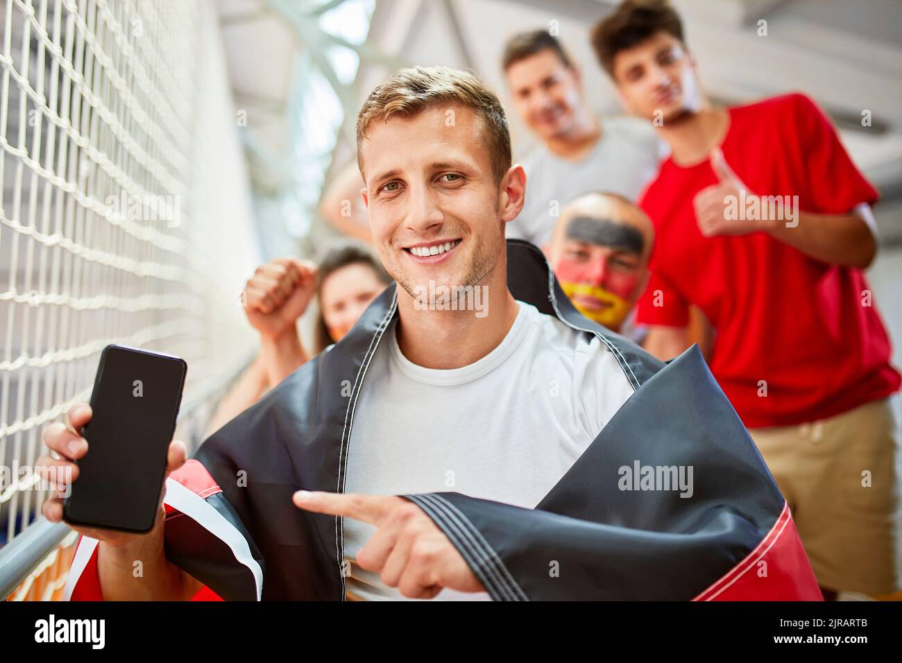 Smiling man with German Flag pointing at smart phone screen at sports ...