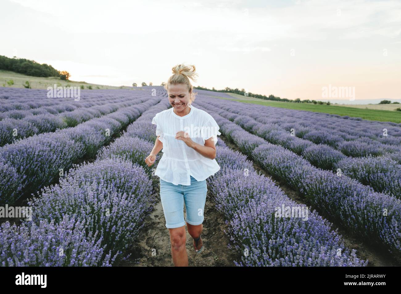 Happy woman running amidst lavender plants Stock Photo - Alamy