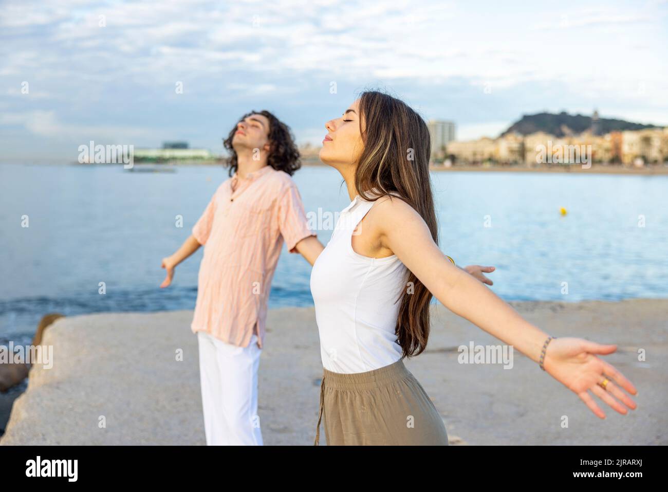 Young couple standing with arms outstretched and eyes closed at pier ...