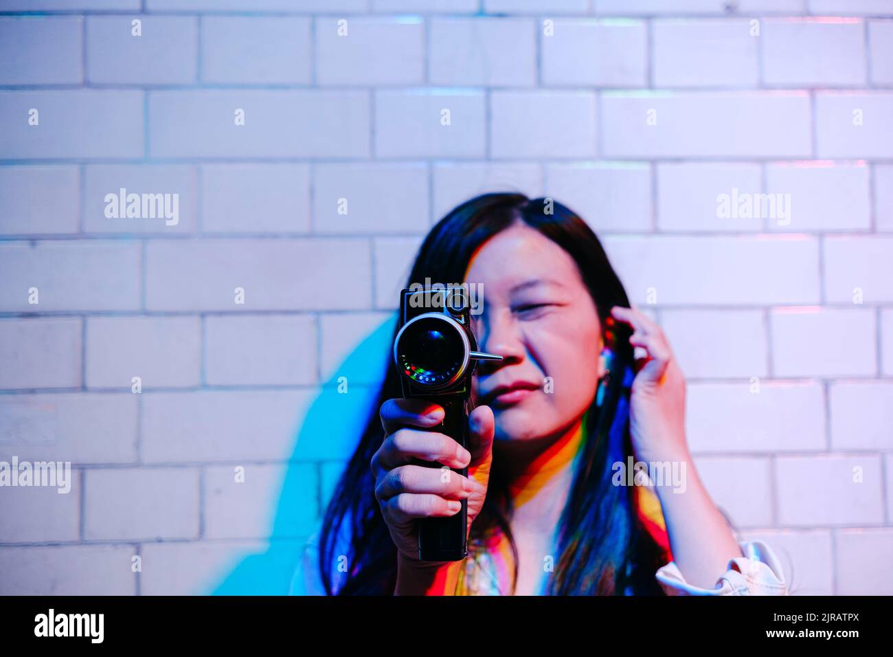 Young woman looking through video camera filming in front of wall Stock ...