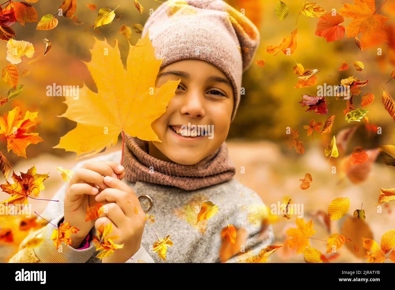 Cute little girl holds an orange maple leaf near the face. Pretty blond ...