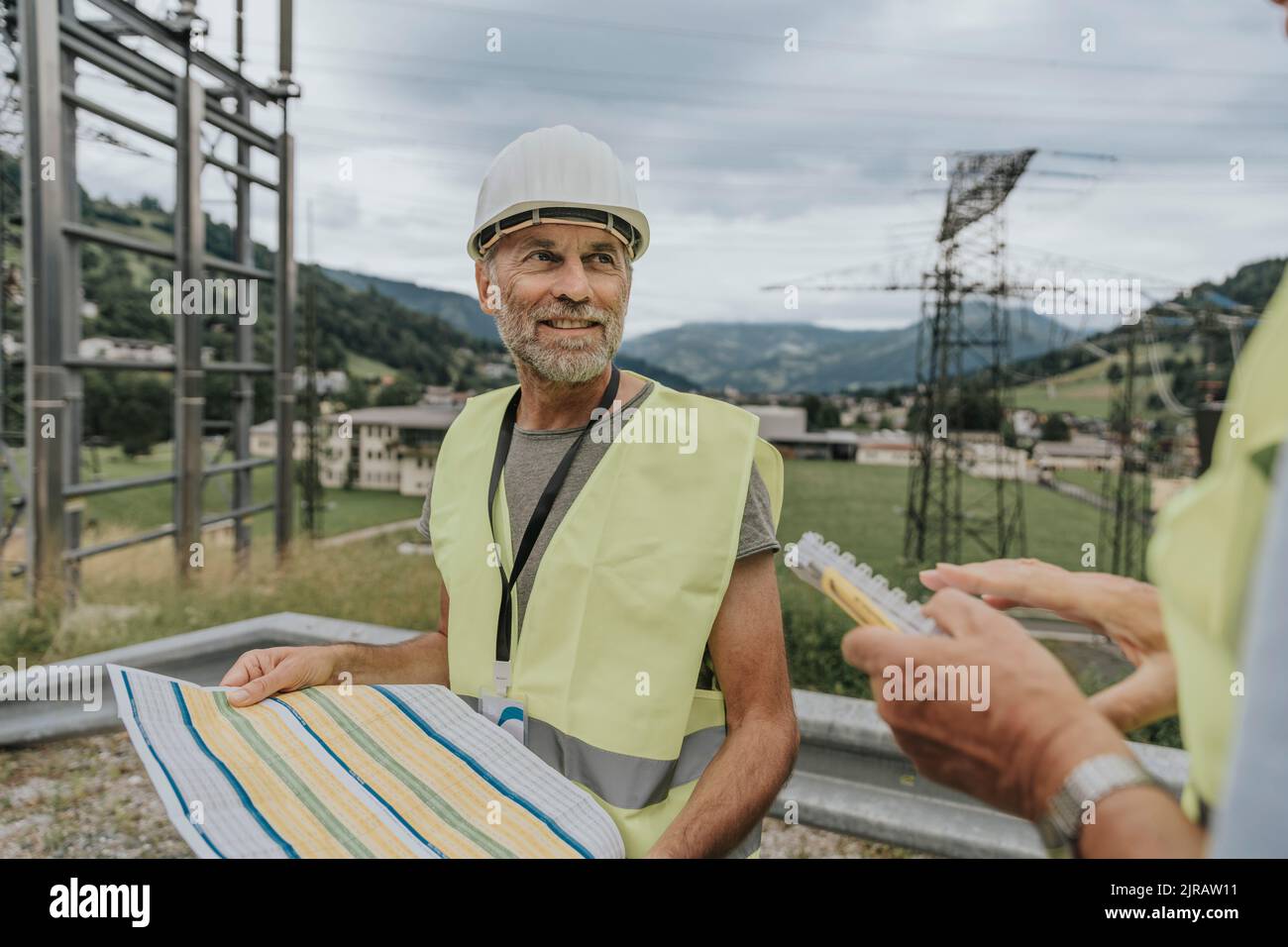 Engineer holding plan listening to coworker at power station Stock ...