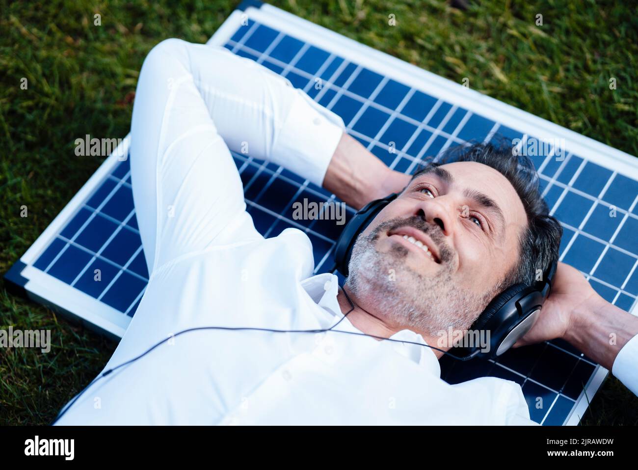 Smiling businessman with hands behind head lying on solar panel ...