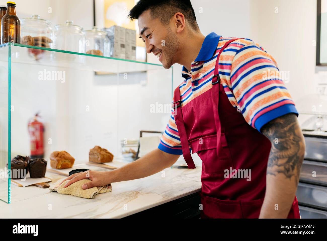 Smiling man cleaning counter with rag in coffee shop Stock Photo - Alamy