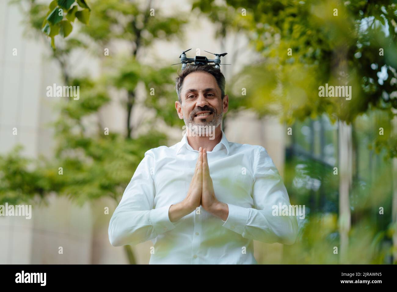 Smiling businessman standing with hands clasped balancing drone on his ...
