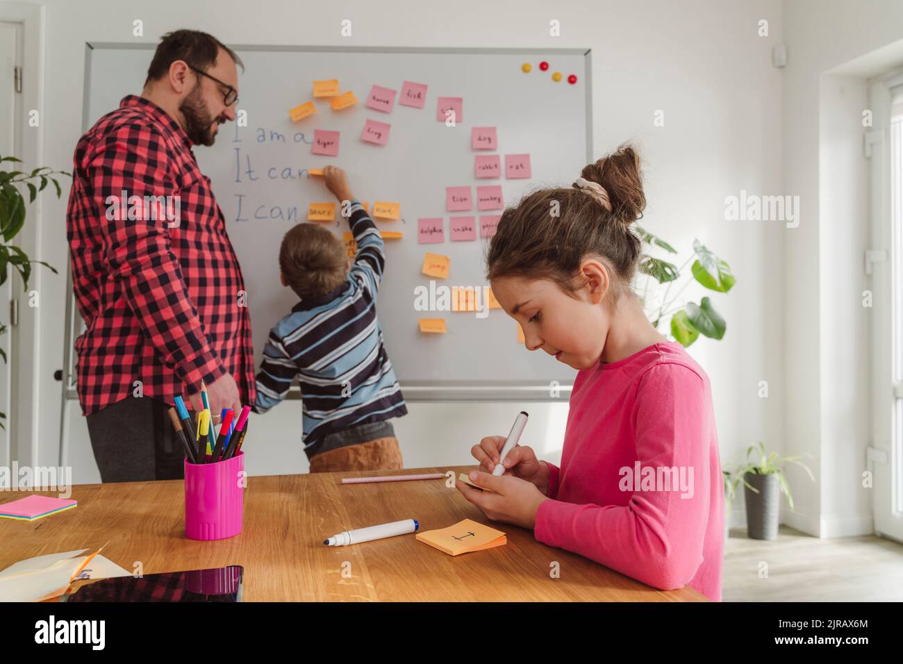 Girl writing with felt tip pen by brother sticking adhesive note on ...