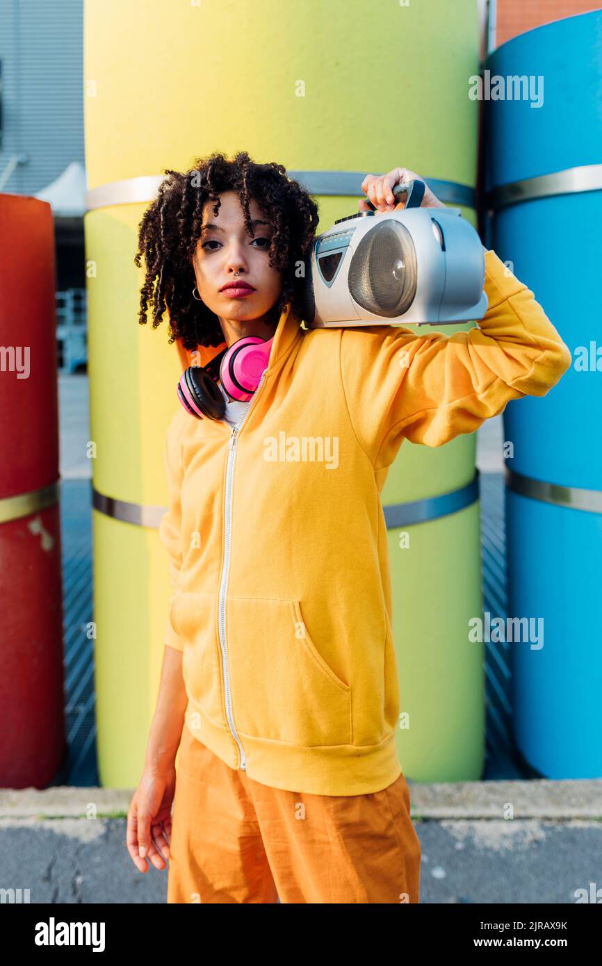 Woman carrying boom box on shoulder standing in front of colorful pipes ...