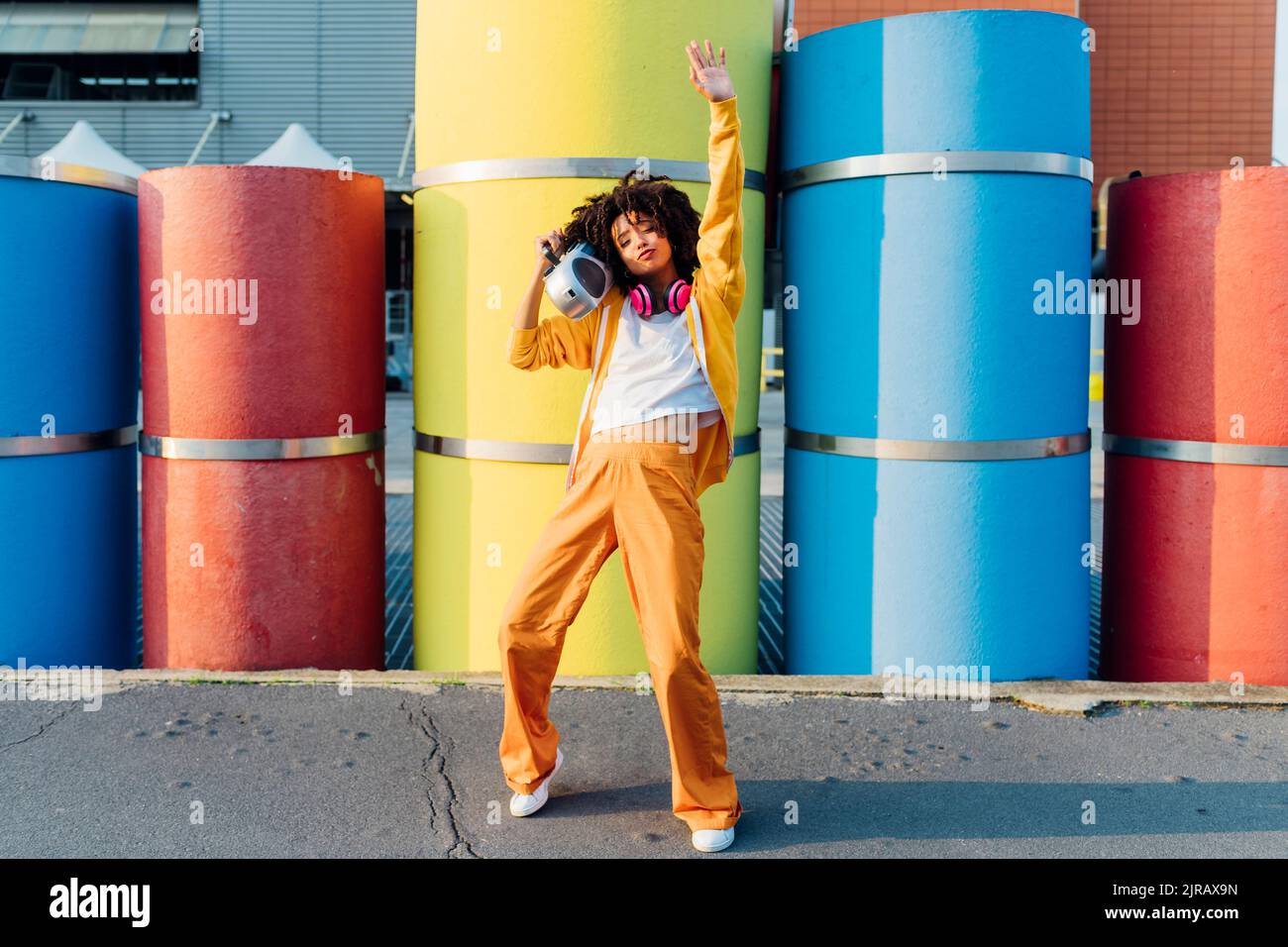 Young woman carrying boom box on shoulder dancing in front of colorful ...